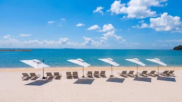 Uma praia com fileiras de espreguiçadeiras e guarda-sóis, céu azul límpido e mar calmo.