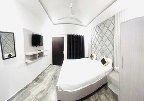 Quarto de hotel moderno com uma cama grande, um ventilador de teto, uma televisão e um guarda-roupa.