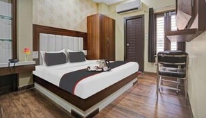 Quarto de hotel com uma cama, uma escrivaninha com cadeira, um guarda-roupa e ar condicionado.