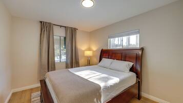 Quarto com cama de madeira, luminária de cabeceira, janela com cortinas e vista para árvores.
