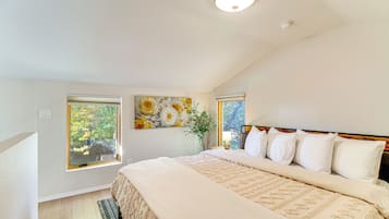 Quarto com uma cama grande, janela com vista para árvores, um quadro na parede e uma luminária no teto.