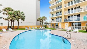 Piscina com espreguiçadeiras e palmeiras, cercada por um edifício de vários andares com varandas.