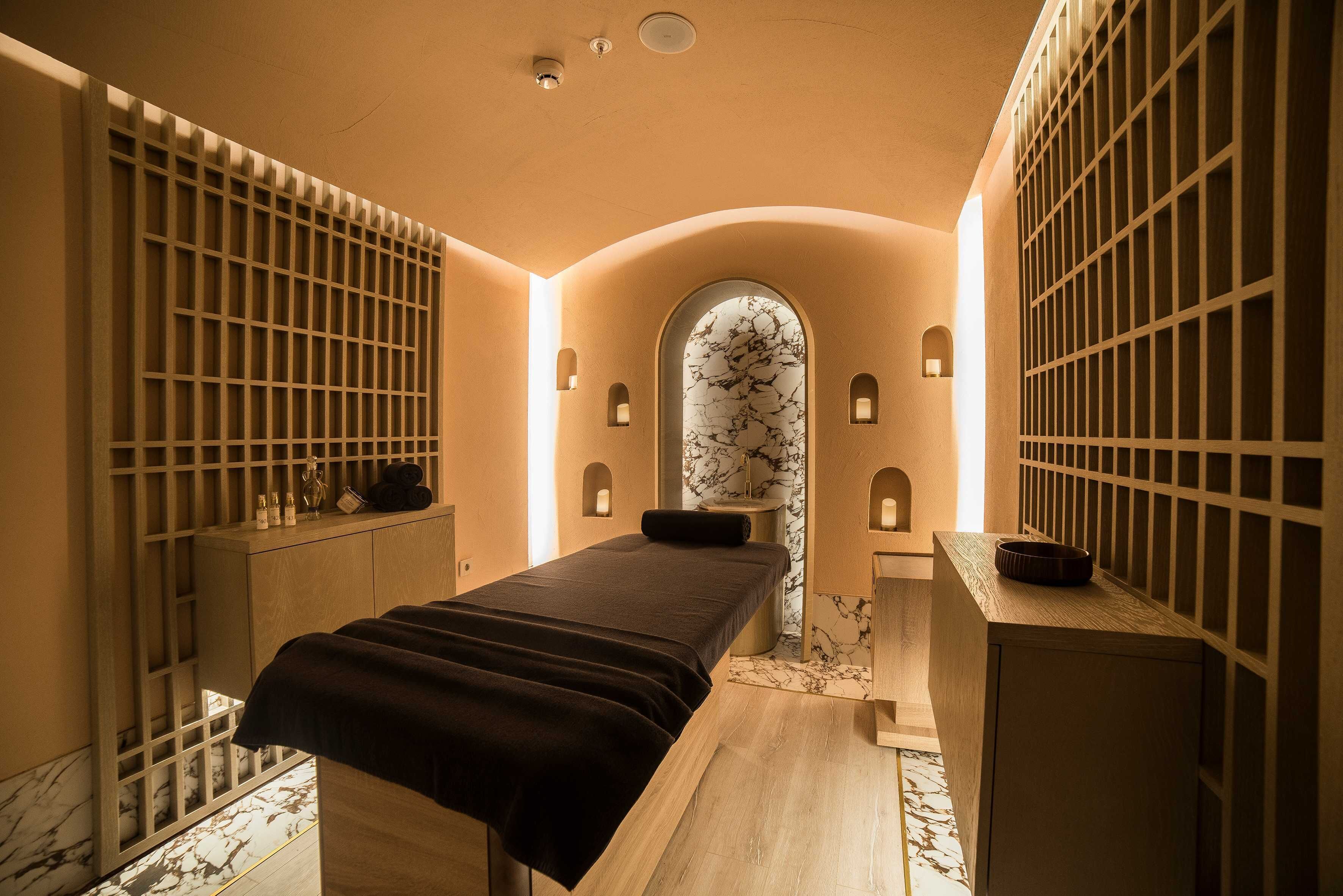 Um espaço de spa com mesa de massagem, armários de madeira e chão de mármore.