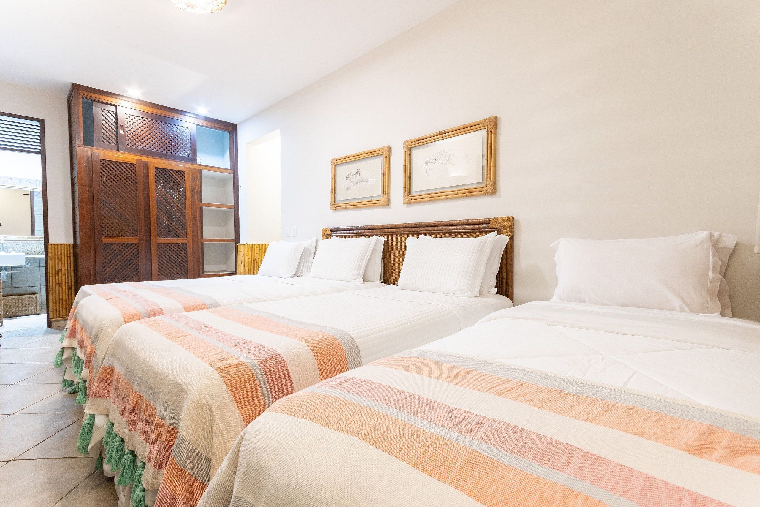 Quarto de hotel com duas camas, um guarda-roupa de madeira e duas imagens emolduradas na parede.