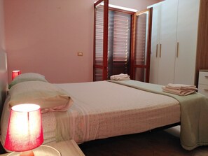 Quarto com cama, mesa de cabeceira, luminária, armário e janela com persianas.