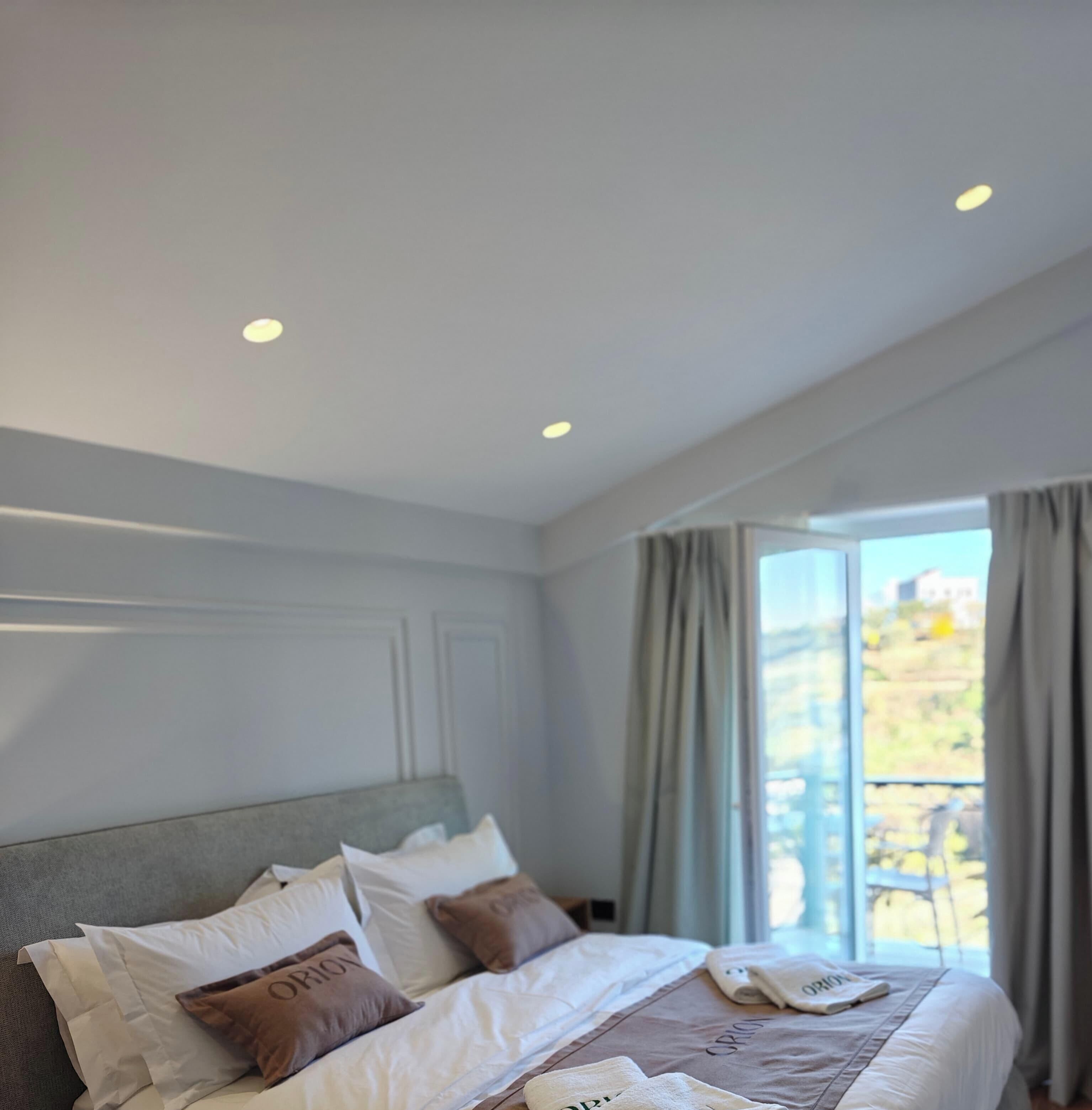Quarto de hotel com cama, cabeceira e janela com cortinas.