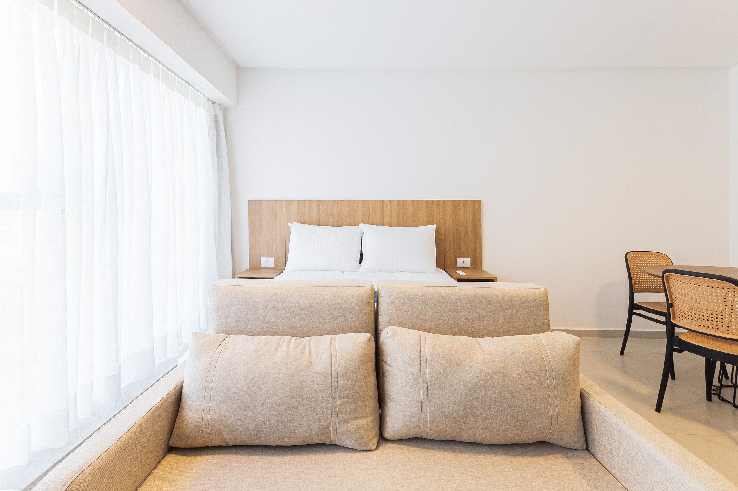 Quarto de hotel moderno com uma cama, duas mesas de cabeceira, uma cadeira e uma mesinha.