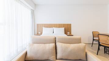 Quarto de hotel moderno com uma cama, duas mesas de cabeceira, uma cadeira e uma mesinha.