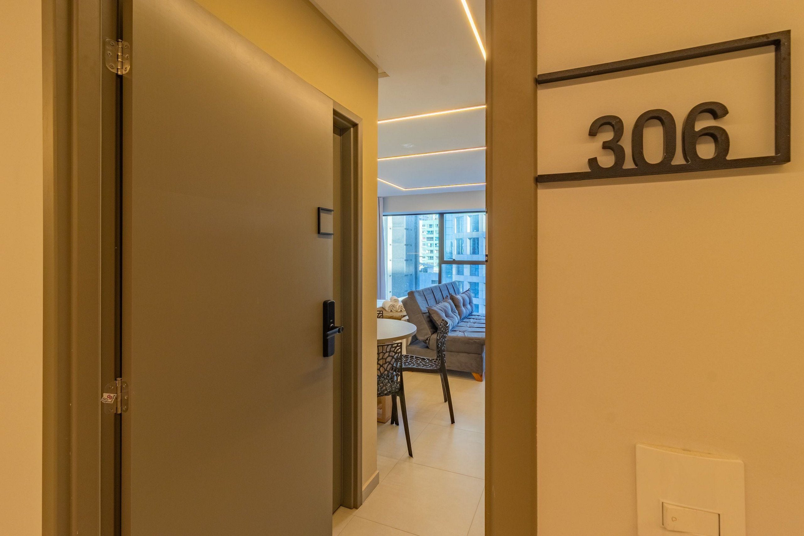Um interior moderno com uma porta que dá para uma sala de jantar e um conjunto de sofás. Uma placa com o número '306' está visível na parede.