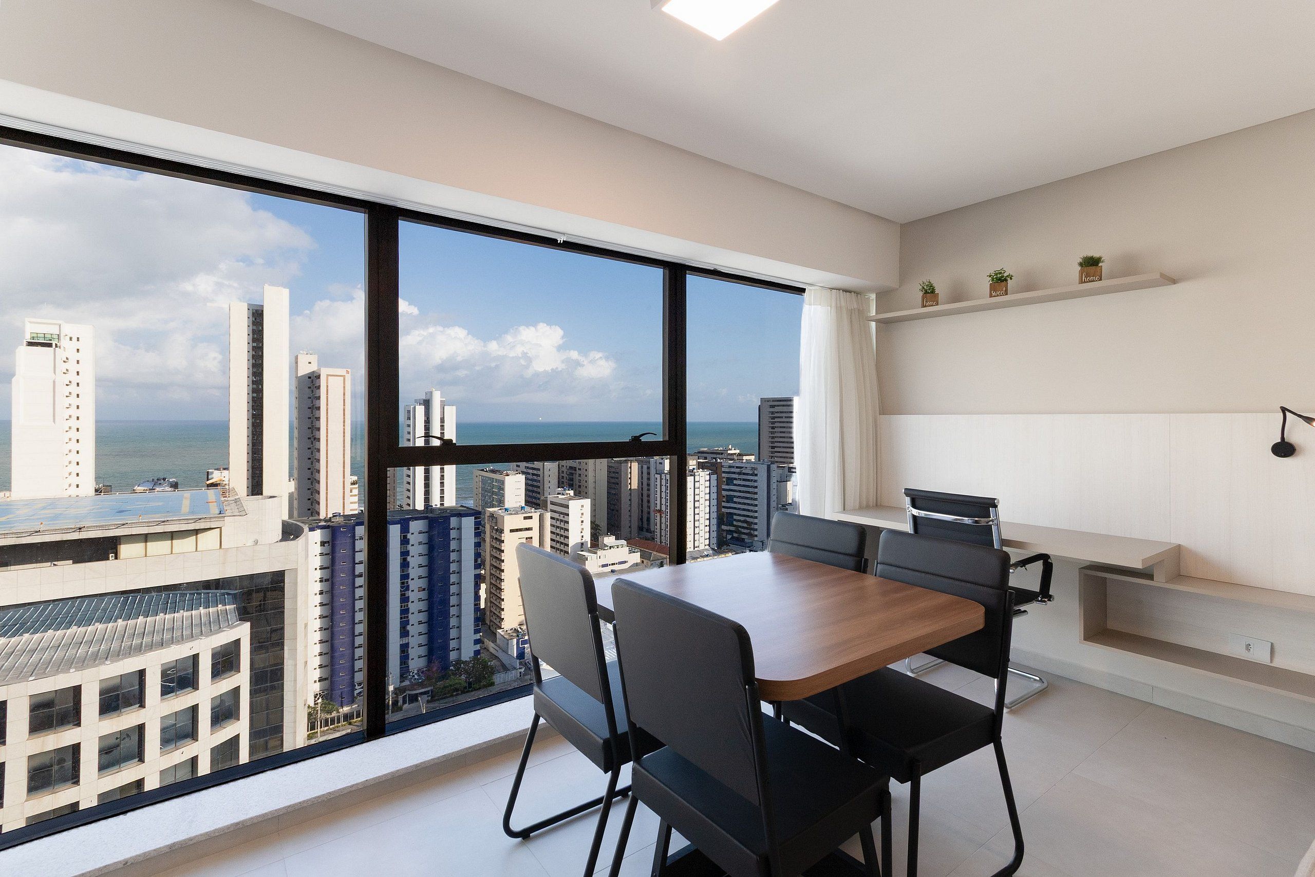 Quarto moderno com uma janela grande, uma mesa de madeira e cadeiras pretas.