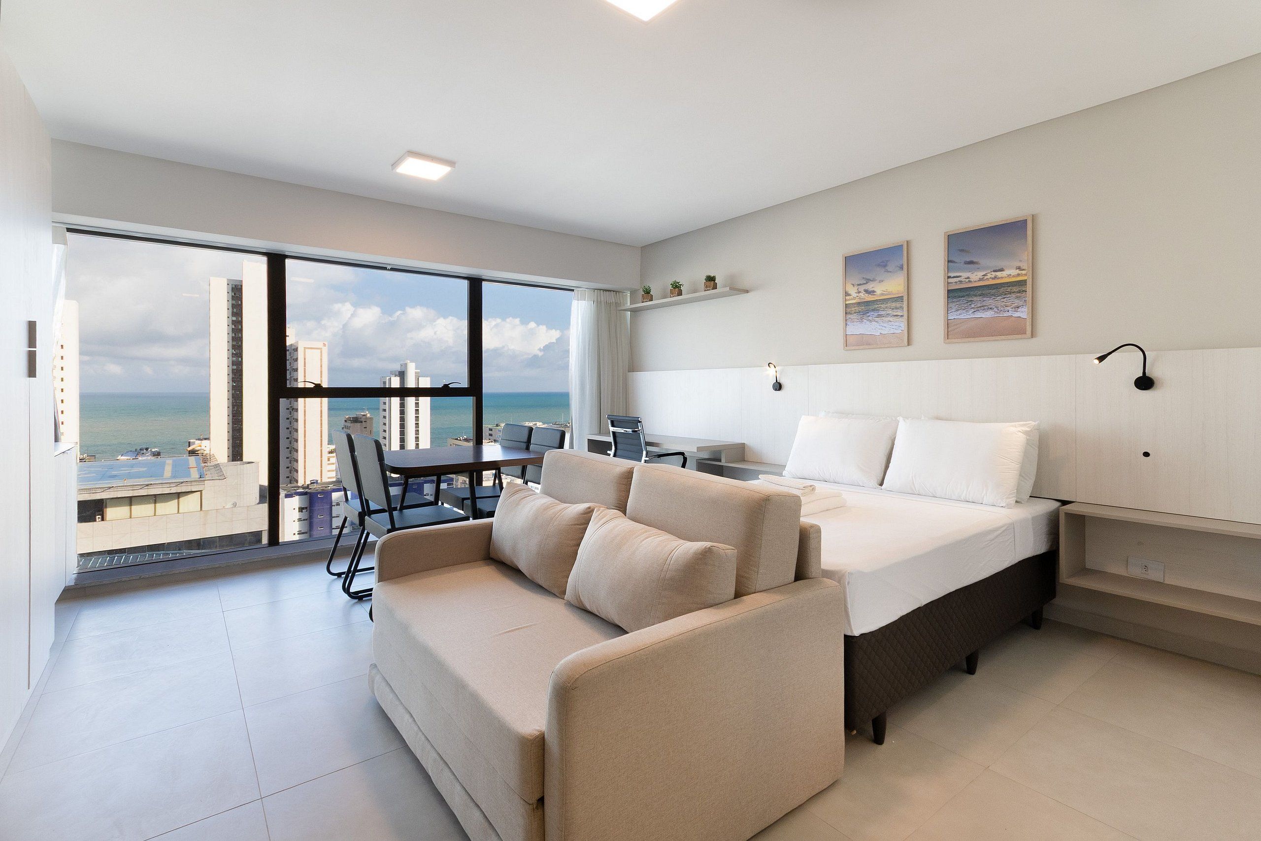 Quarto de hotel moderno com varanda, sofá, cama e área de refeições.