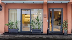 Entrada de hotel com grandes portas de vidro, plantas em vasos e uma placa com a inscrição 'Villa Noem'.