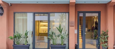 Entrada de hotel com grandes portas de vidro, plantas em vasos e uma placa com a inscrição 'Villa Noem'.
