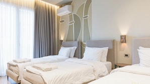Quarto de hotel com três camas, uma janela grande com cortinas e um design moderno na parede.