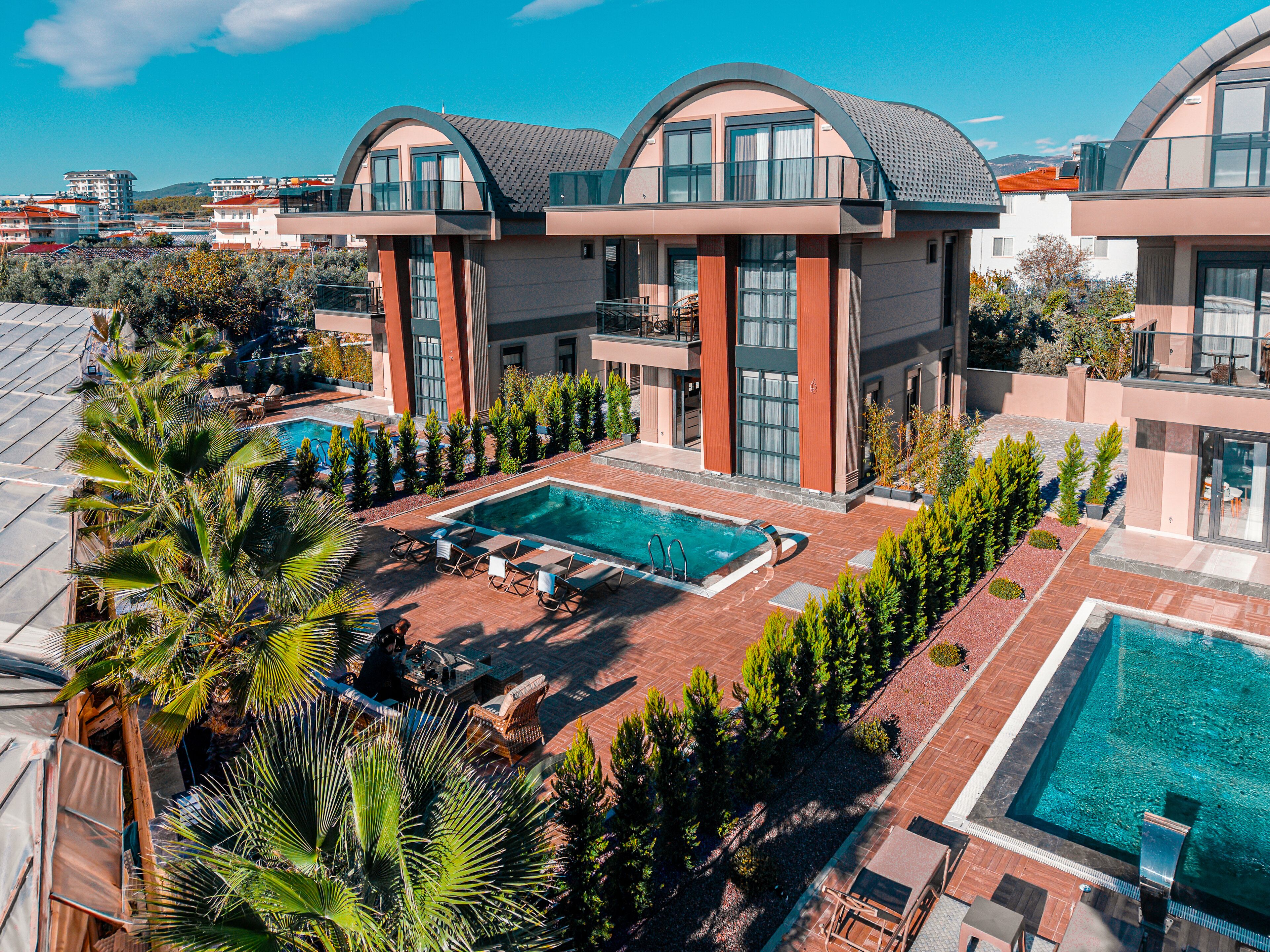 Um hotel moderno com piscina no terraço, várias varandas e um jardim paisagístico.