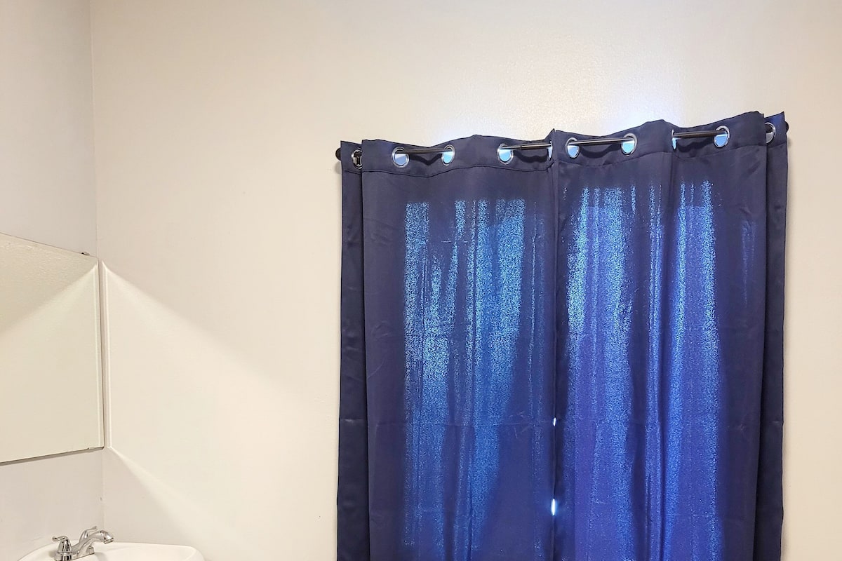 Um banheiro com pia branca, cama amarela e cortina de chuveiro azul.