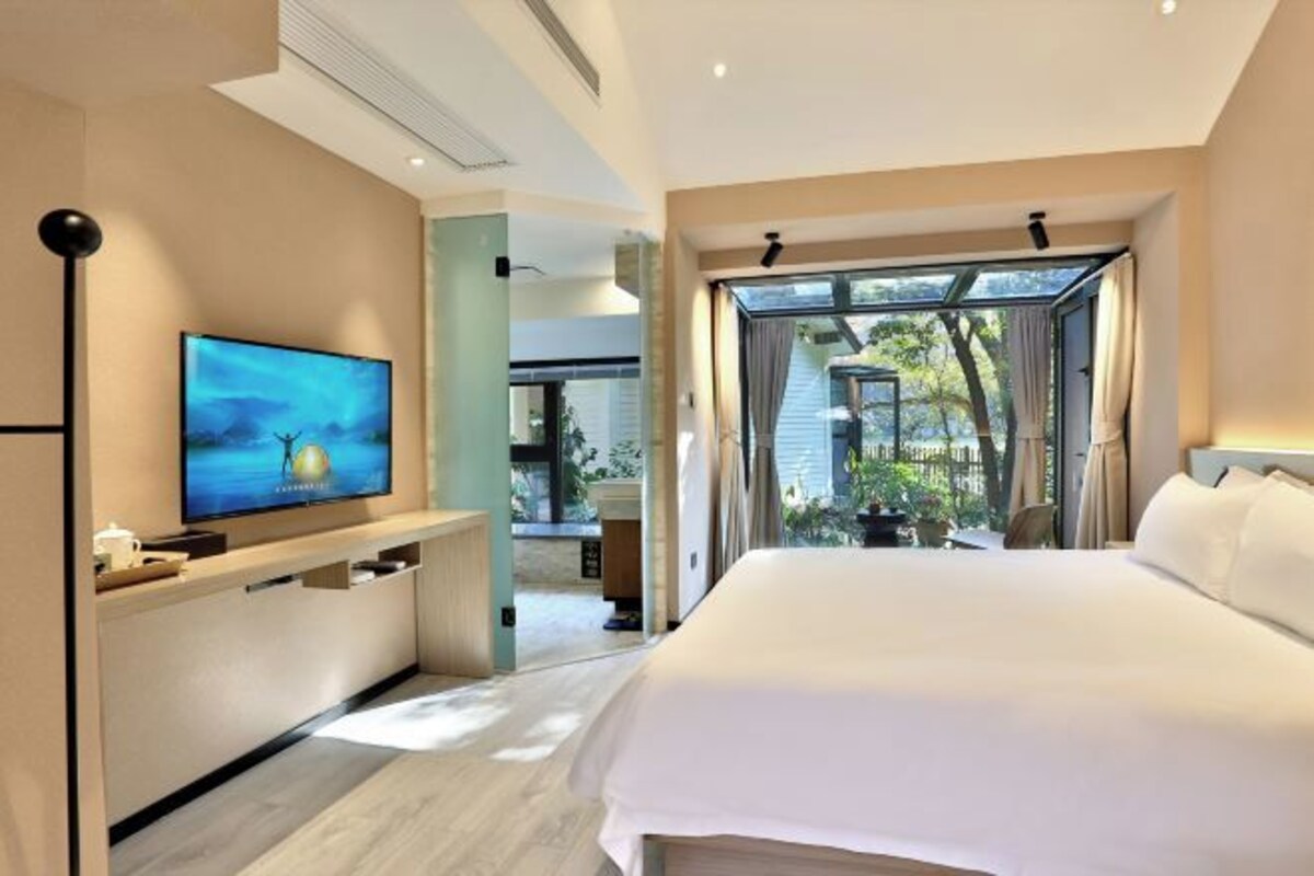 Quarto de hotel moderno com uma cama grande, televisão de tela plana e vista para o exterior.