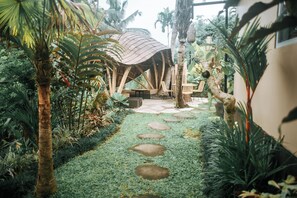 Um jardim tropical com um caminho de pedra, uma estrutura de madeira e vegetação exuberante.
