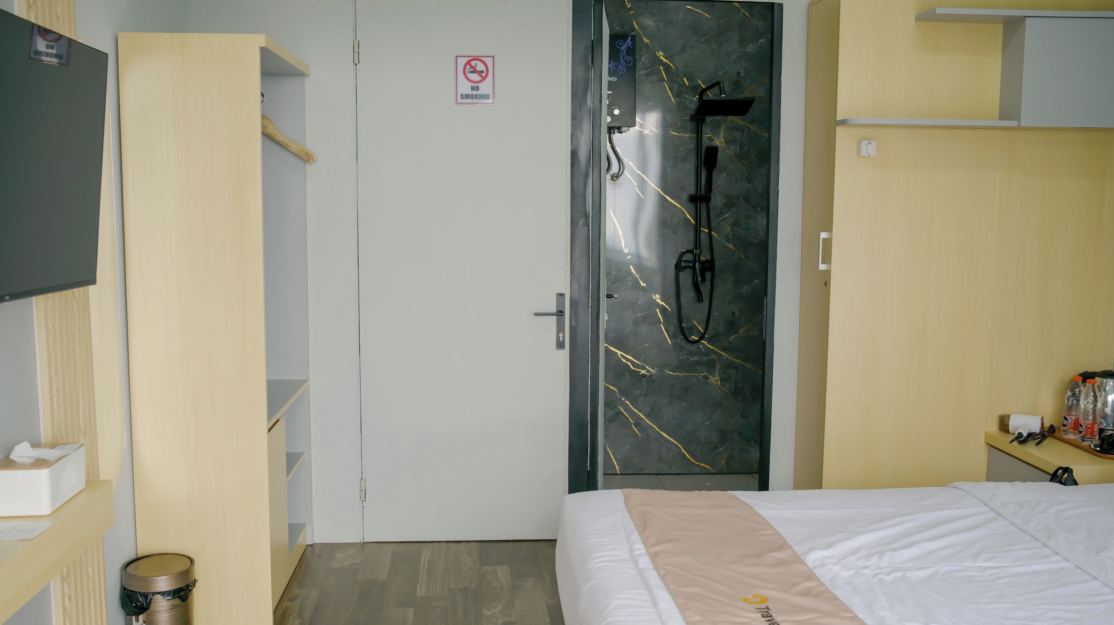 Quarto de hotel com cama, guarda-roupa, área de chuveiro e televisão.