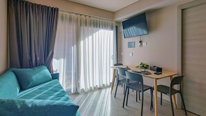 Quarto moderno com sofá, mesa de jantar com cadeiras, TV fixada na parede e janela com cortinas.