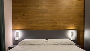 Uma cama com lençóis brancos, cabeceira de madeira e duas luminárias de apoio.