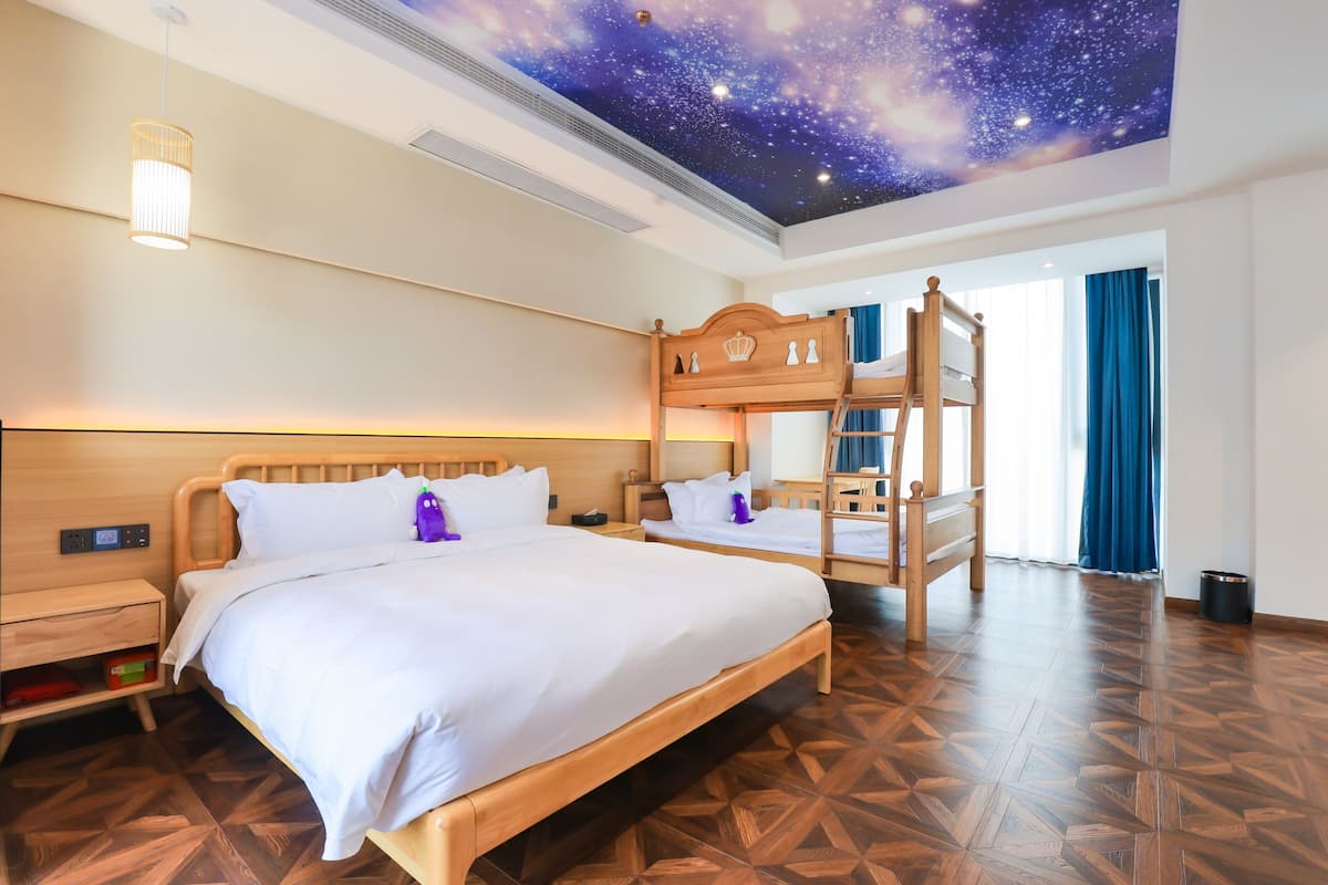 Quarto de hotel com uma cama grande, uma beliche de madeira, uma mesinha de cabeceira e um teto com desenho de céu estrelado.