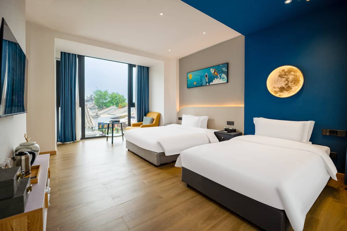 Quarto de hotel moderno com duas camas, uma escrivaninha e vista para o exterior.