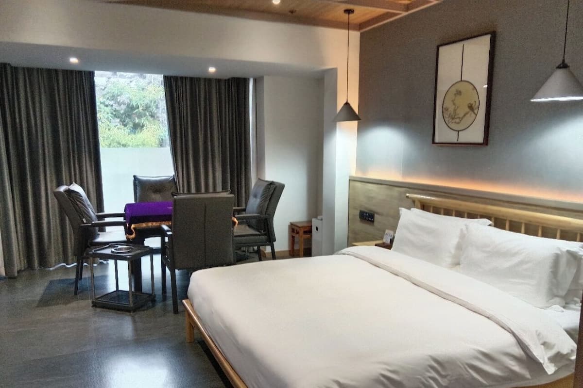 Quarto de hotel com uma cama grande, duas cadeiras, uma mesa pequena e vista pela janela.