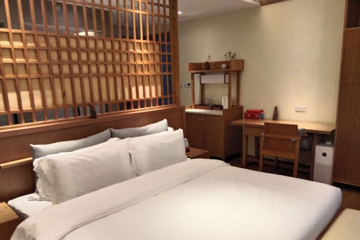 Quarto de hotel com uma cama, uma escrivaninha, uma cadeira e um painel de madeira.