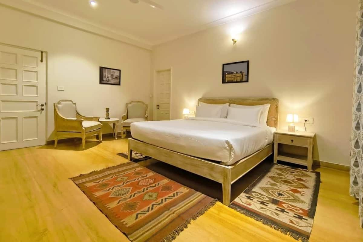 Quarto com uma cama grande, duas mesas de cabeceira, uma cadeira e uma mesinha.