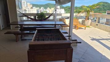 Uma área externa com mesa de pebolim, bancos e rede.