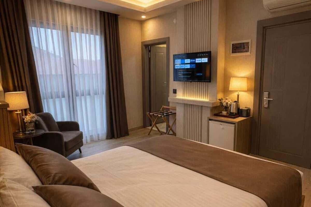 Quarto de hotel com cama grande, escrivaninha com luminária, televisão e armário.