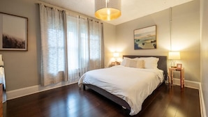 Quarto com uma cama grande, duas mesas de cabeceira com luminárias, um lustre e uma janela com cortinas.