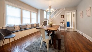 Uma sala de estar espaçosa com uma mesa de jantar de madeira, um banco embutido com almofadas, uma escada e vista para o exterior.