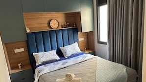 Cama bem arrumada com relógio, duas almofadas, um cobertor e uma toalha.