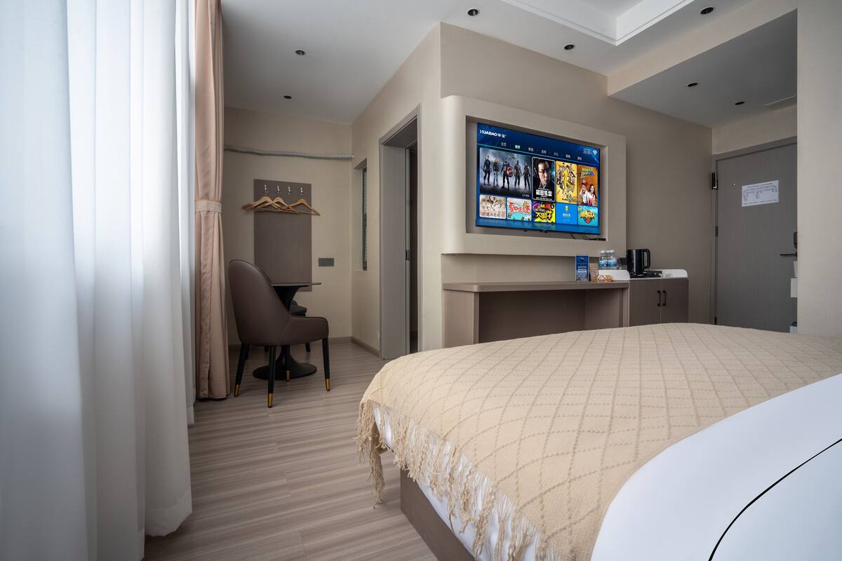 Quarto de hotel com cama, escrivaninha, televisão na parede e porta.
