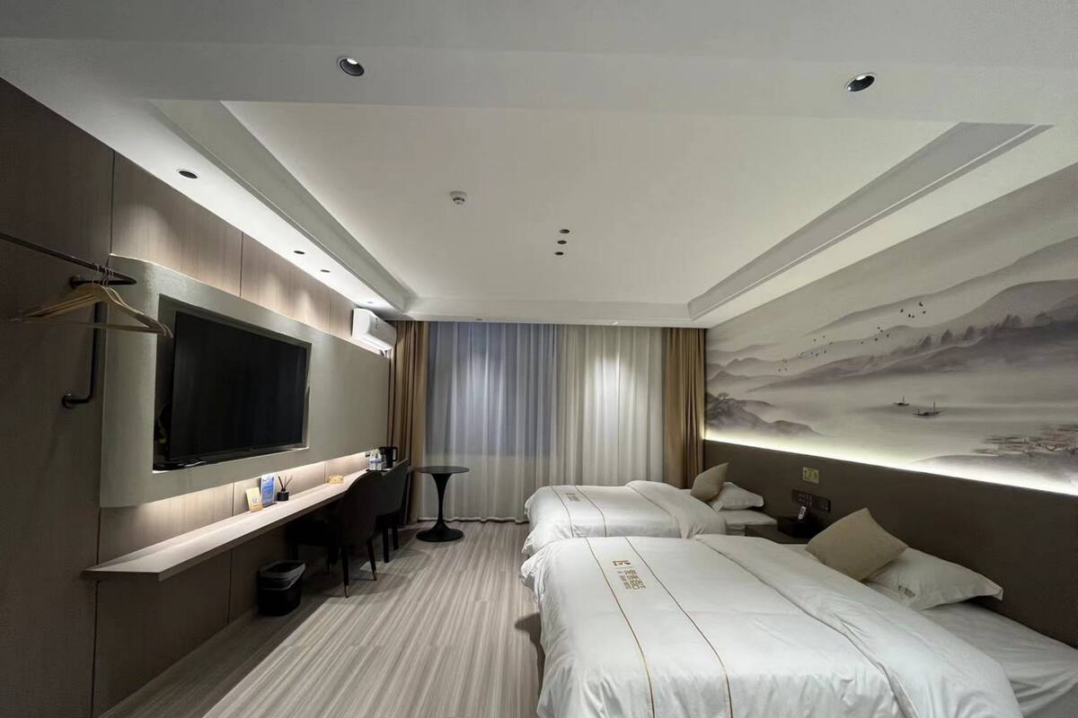 Quarto de hotel moderno com uma cama grande, uma escrivaninha com televisão de tela plana, uma mesinha e um quadro na parede.