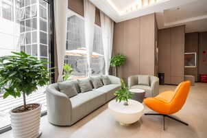 Uma sala de estar moderna com um sofá cinzento, uma poltrona laranja e duas plantas em vasos.