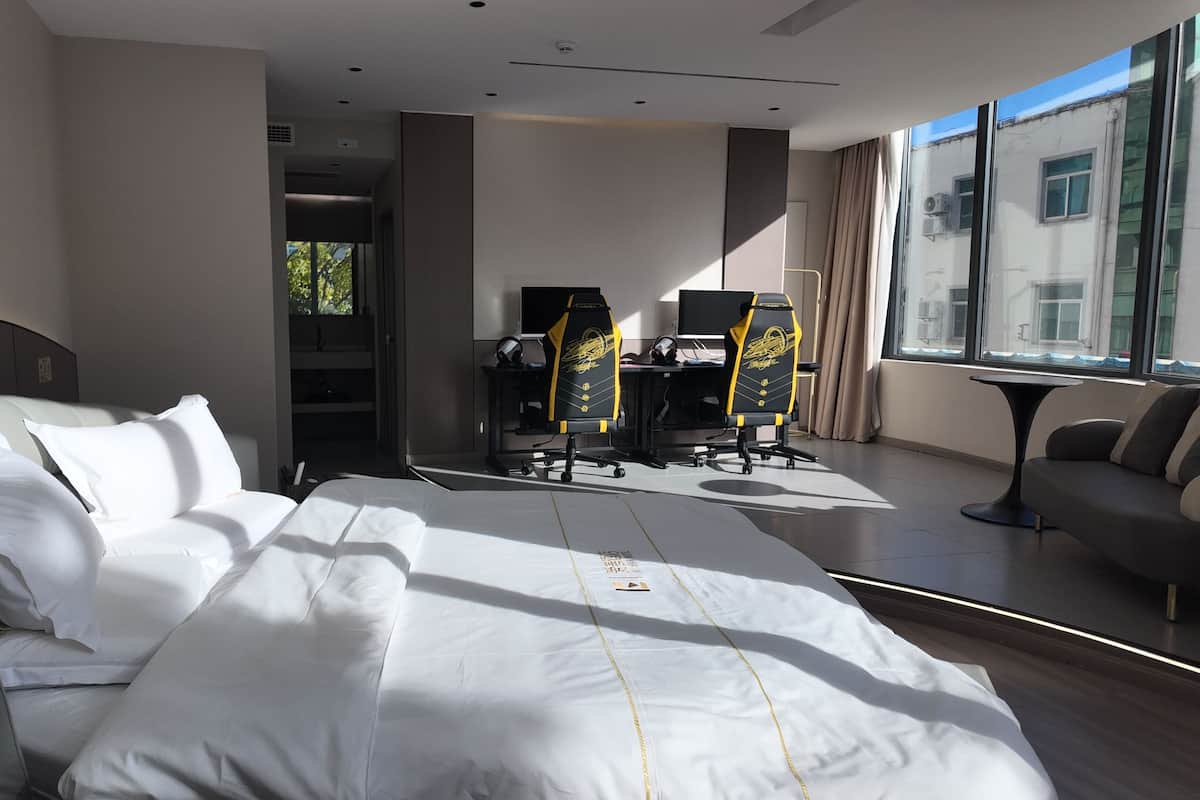 Quarto de hotel moderno com uma cama grande, uma escrivaninha com computador e vista para a cidade através de amplas janelas.