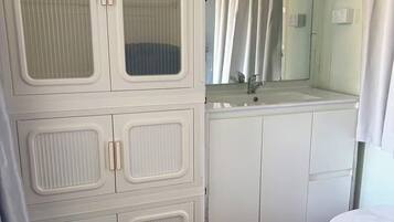 Uma casa de banho com um armário branco, um espelho, uma pia e uma sanita.