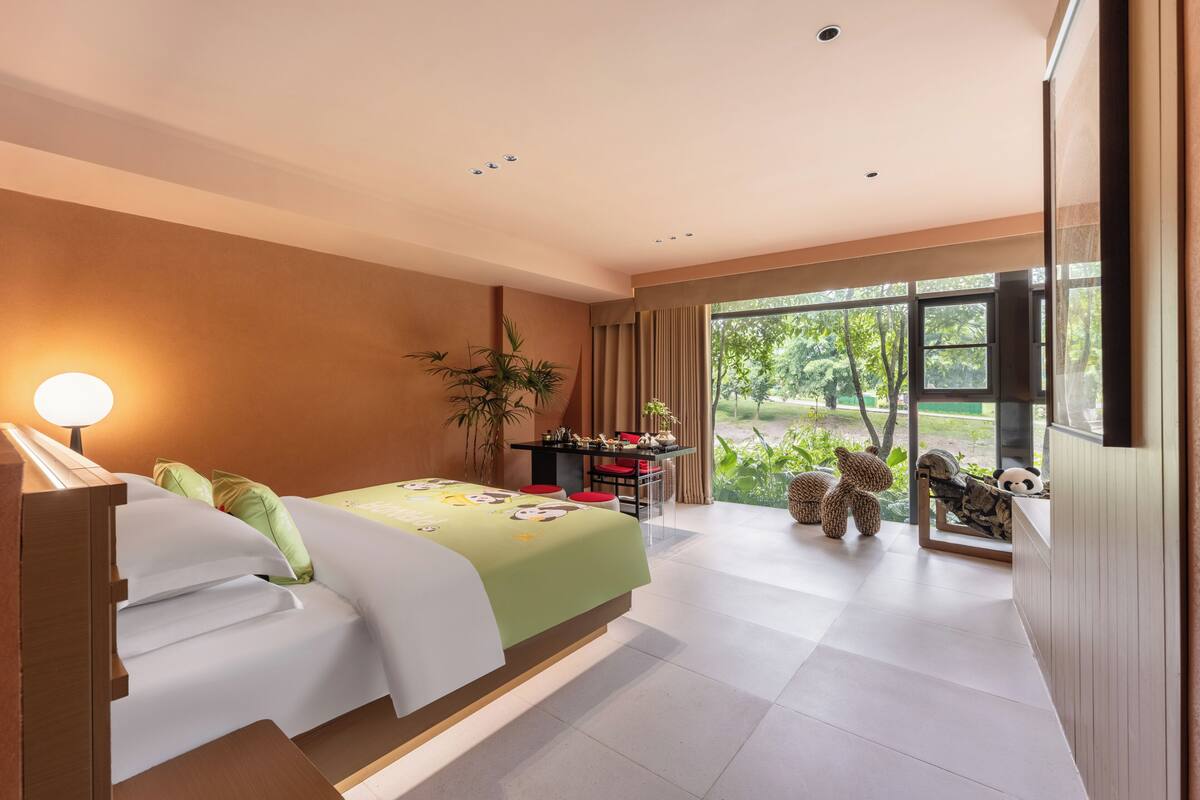 Quarto de hotel moderno com uma cama grande, uma escrivaninha e vista para o exterior.
