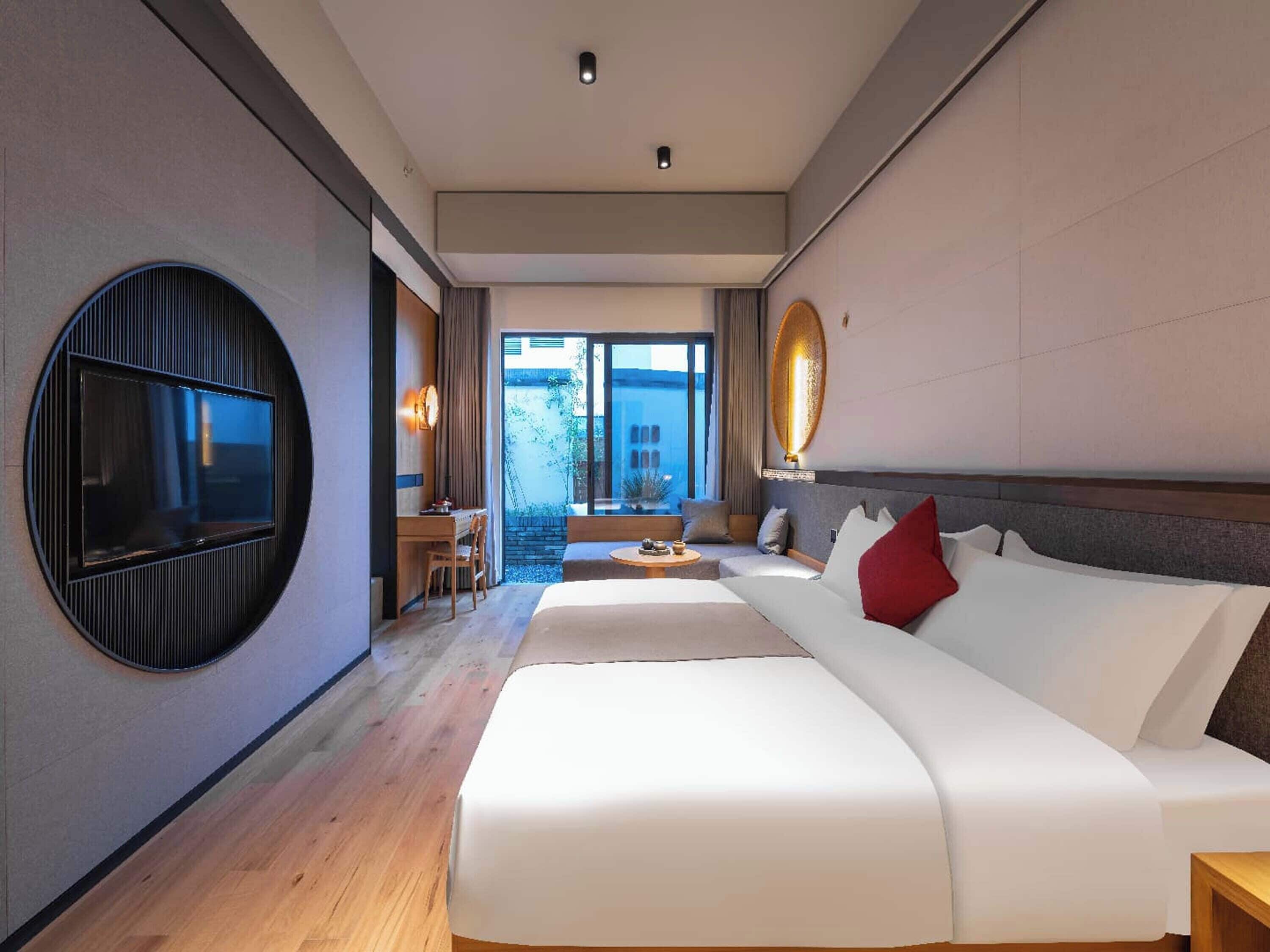 Quarto de hotel moderno com duas camas, televisão, escrivaninha e vista para o exterior.