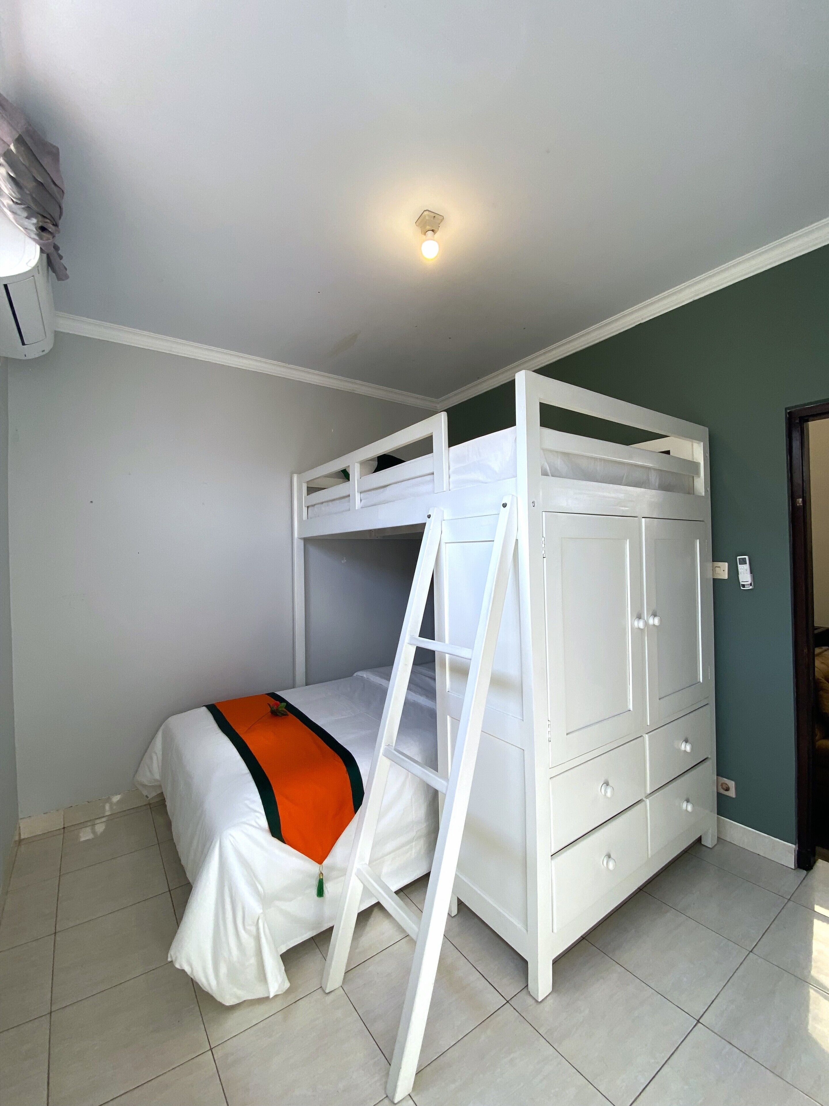 Uma cama beliche com escada, gavetas brancas e um cobertor branco com detalhes em laranja.