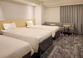 Quarto de hotel com três camas, um sofá e duas mesinhas.