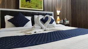 Quarto de hotel com uma cama bem arrumada, uma fotografia enquadrada de um elefante na parede e uma toalha dobrada em formato de coração na cama.
