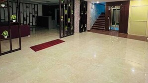 Um hall amplo com piso de mármore, balcão de recepção, escada e plantas decorativas.