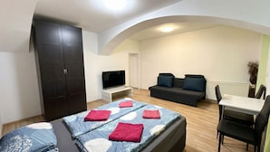 Quarto compacto com cama, sofá, televisão e mesa de jantar.