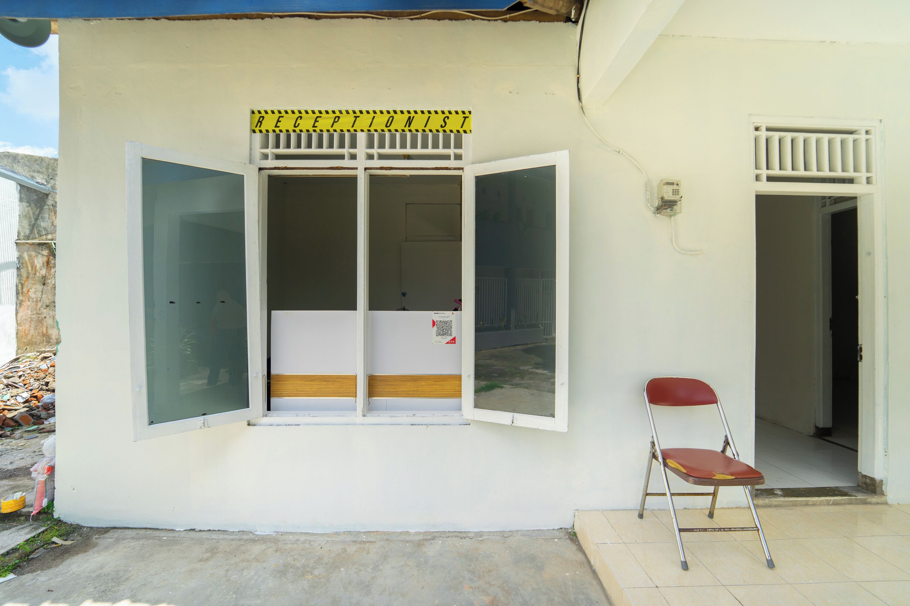 Um edifício branco com uma janela e uma porta, uma cadeira vermelha do lado de fora e fita de isolamento amarela na janela.