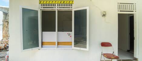 Um edifício branco com uma janela e uma porta, uma cadeira vermelha do lado de fora e fita de isolamento amarela na janela.