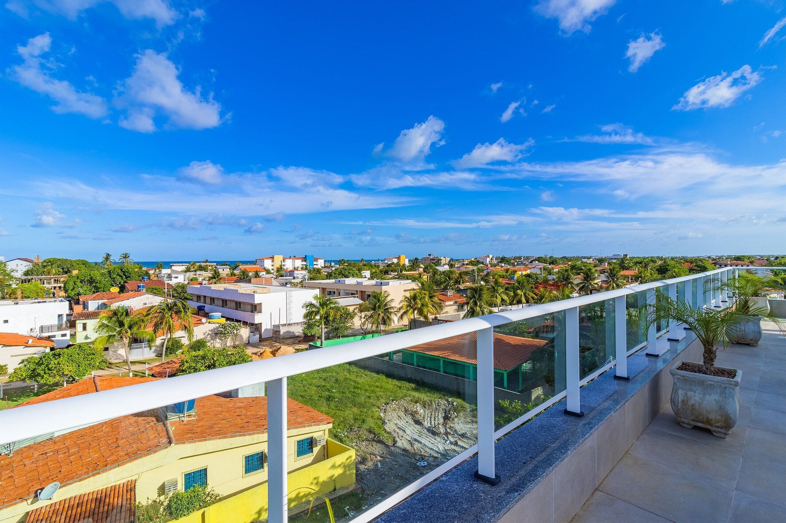Varanda com vista clara para uma cidade costeira, com uma mistura de edifícios residenciais e palmeiras.
